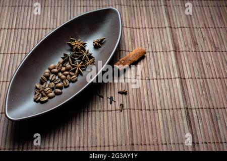 Brown canoe-shaped dish on bamboo mat with coffee beans, star anise ...