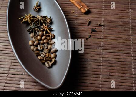 Brown canoe-shaped dish on bamboo mat with coffee beans, star anise ...