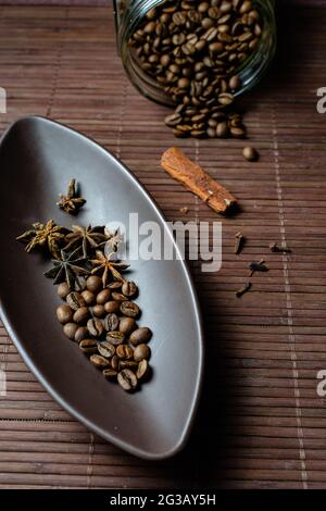Brown canoe-shaped dish on bamboo mat with coffee beans, star anise ...