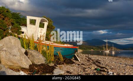 Small shipwreck at a loch with stone beach Stock Photo - Alamy