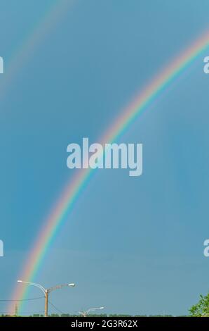 Beautiful partial rainbow on the blue sky above the green field and ...