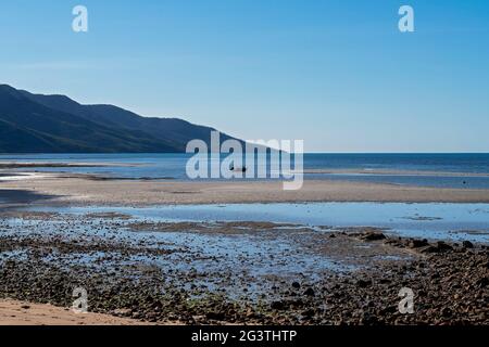 Muddy rocky seabed at low tide with small boat anchored offshore Stock ...