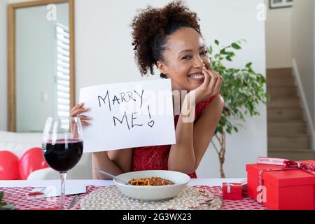 African american woman holding placard with marry me text on videocall ...