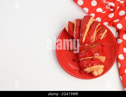 two baked croissants with cherry glaze on a red ceramic plate, white ...