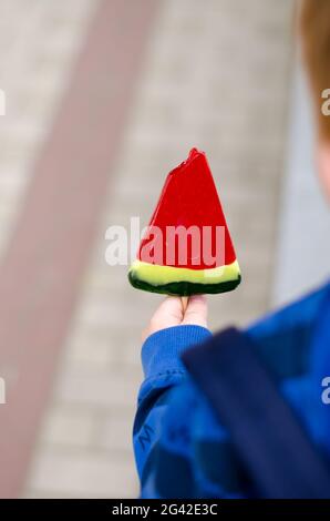 Child's hand holding lollipop in the shape of piece of watermelon ...