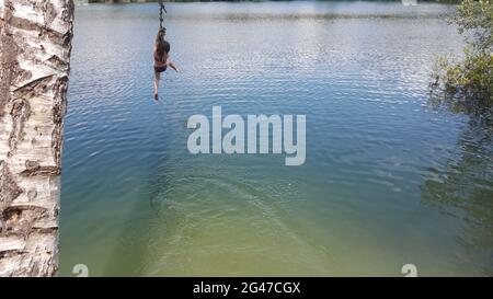 Cool shot of a female jumping into the lake with a rope hanging on the ...