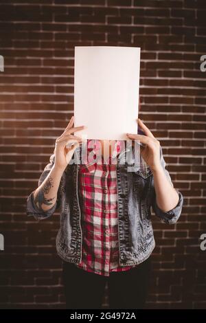 Woman hiding face from blank sheet against brick wal Stock Photo - Alamy