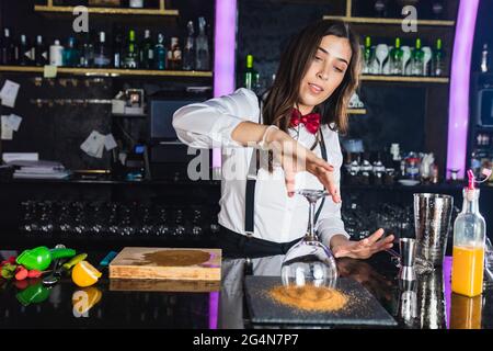 Female barkeeper in stylish outfit adding ice cubes into a glass while ...