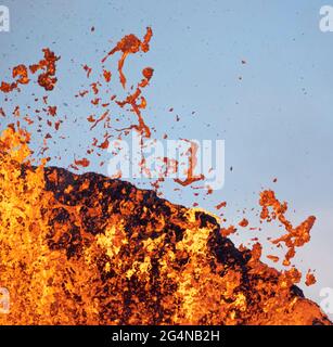 Splashes of hot orange lava erupting from volcanic mountain peak ...