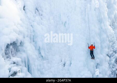 Male athlete doing a vertical ice climb, kicking front crampons into ...