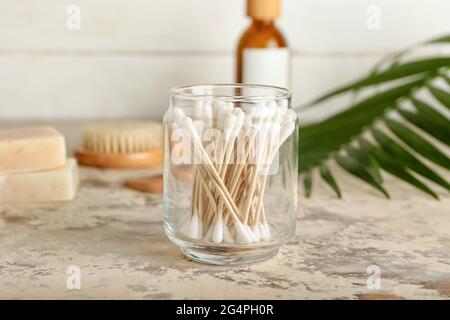 Glass jar with cotton swabs and tropical leaf on color background Stock ...