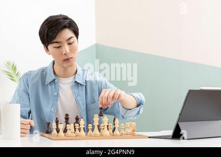 Asian young man learning chess through online class using tablet device ...