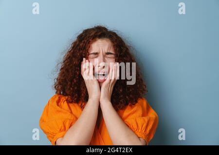 Scared ginger woman screaming and touching her face isolated over blue ...