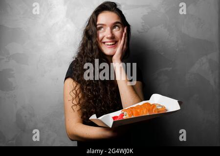 Surprised girl with sushi set philadelphia rolls in a paper box happy ...
