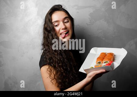 Surprised girl with sushi set philadelphia rolls in a paper box happy ...