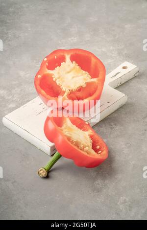 one fresh halved red bell pepper on a wooden cutting board on gray ...
