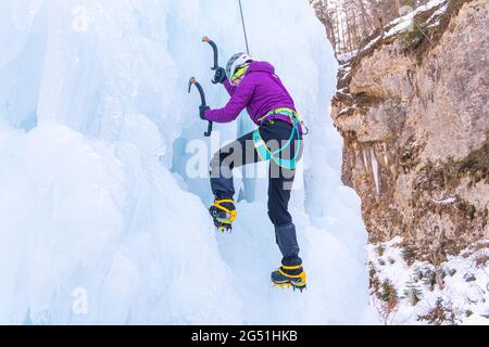 Woman climbing down the side of an icy slope, hanging on a rope ...