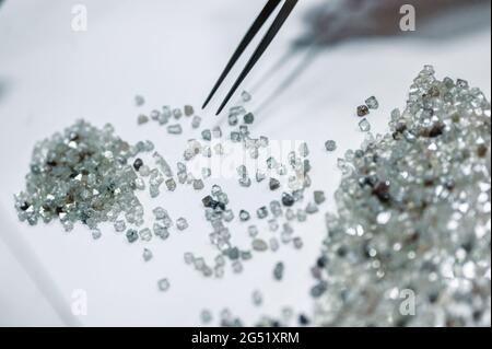 A hand holding tweezers transfers diamonds from one pile to another ...