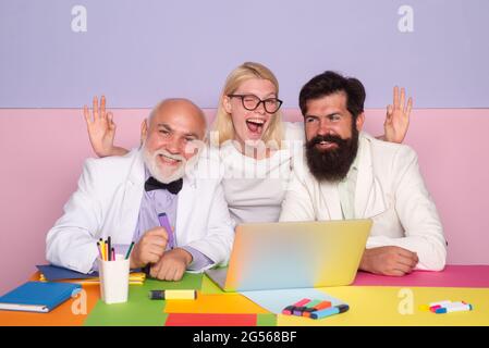 Funny excited business team sitting by the table with laptops ...