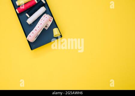 Pack of colorful sewing threads and a measuring tape on orange ...