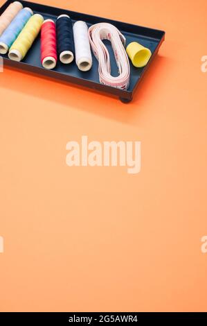 Pack of colorful sewing threads and a measuring tape on orange ...