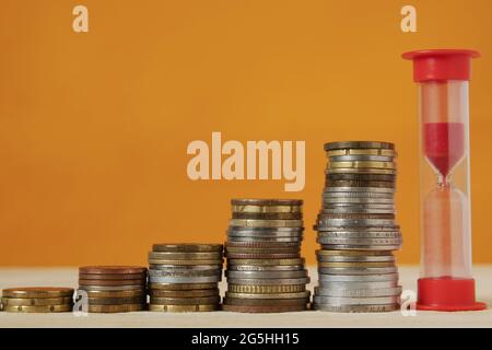 A pyramid of stacks of coins at the head of which is an hourglass. The ...