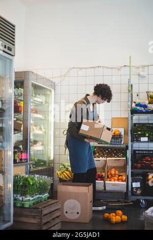 Young male owner standing with fruit basket in deli store Stock Photo ...