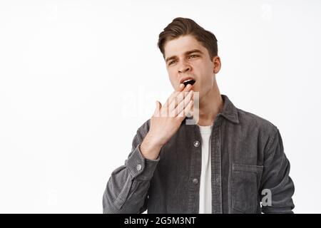 Uninterested young stylish man yawning as hear boring conversation ...