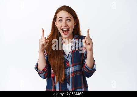 Excited beautiful girl smiling and pointing fingers aside isolated over ...
