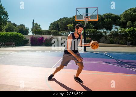 A male basketball player trains himself on a basketball court with a ...