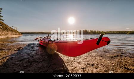 Close up view of red kayak at wet river coastline with green forest at ...