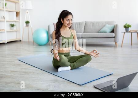 Beautiful Indian woman meditating to online video on laptop computer at ...
