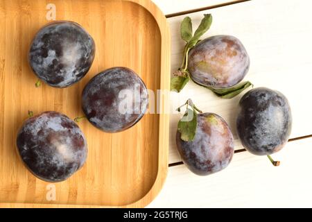 Several organic plums on a bamboo plate, close-up, isolated on a black ...