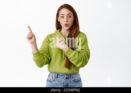 Excited redhead girl pointing fingers sideways, showing two choices and ...