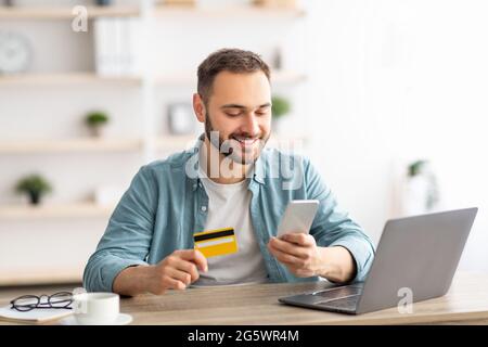 Happy Caucasian man buying things online, using smartphone and credit ...