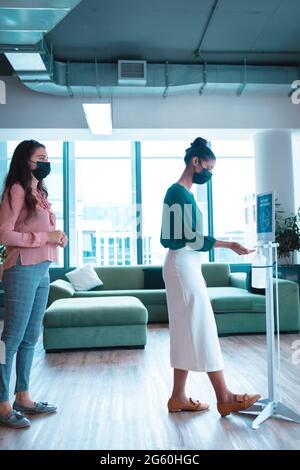 Two diverse businesswomen wearing face masks, holding tablet and ...