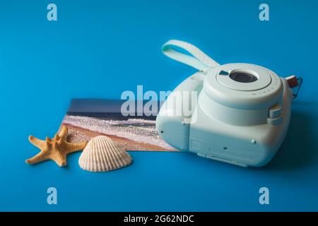 Camera, seashells and postcard with sea view on a blue background ...