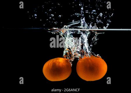 two tangerines fall into the water on a black background, copy space ...