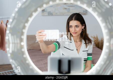 pretty and positive fashion blogger taking selfie near clothes and ...