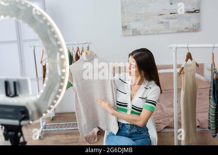 blurred phone holder with ring lamp near fashion blogger holding tag ...