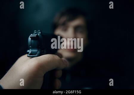 First person view of gun aimed at young man on dark background. POV of ...