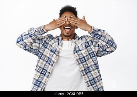 Happy smiling guy waiting for surprise, covering eyes with hands and ...