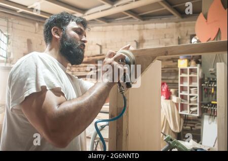 Craftsman is using an electric sander, to smoothen the wood texture ...