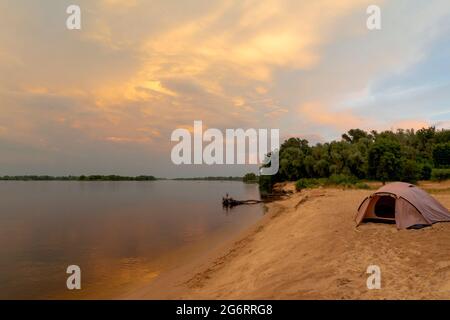 Tourist tent on the high bank of the river at sunset. Beautiful summer ...