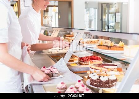 Women in pastry shop filling up sales display with pies Stock Photo - Alamy