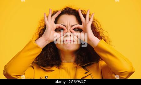young curly woman imitating eyeglasses with hands and sticking out ...