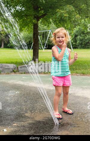 Happy smiling child playing at splash pad with water. Little girl ...