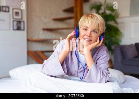 Smiling blonde woman listens to music while showcasing modern denim ...