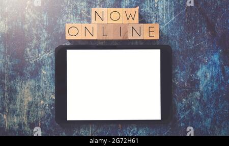 Now Online in Block Letters on a Blue Wooden Table with a Blank Tablet ...