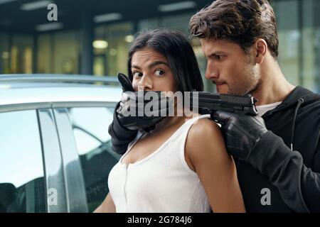 Angry robber closing mouth and threatening with pistol to frightened ...